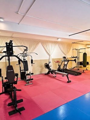 Academia com diversos equipamentos de ginástica, incluindo um banco de musculação, bicicleta ergométrica e esteira.