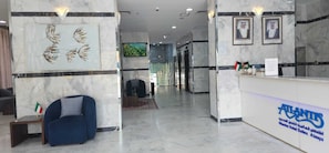 Um saguão de hotel com paredes de mármore, uma mesa de recepção e uma área de estar com um sofá azul.