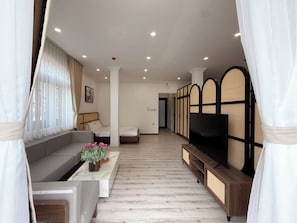 Quarto de hotel moderno com sofá, televisão, piso de madeira e cama.
