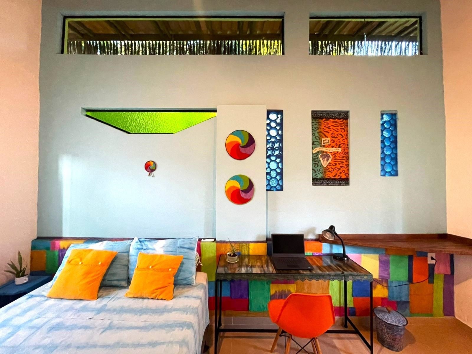 Quarto com cama, escrivaninha, cadeira e obras de arte nas paredes.