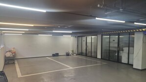 Um espaço amplo e coberto, com piso plano, um banco de metal e uma lixeira.