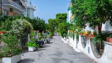 Uma rua estreita ladeada por edifícios residenciais, alguns com varandas e vasos de plantas.