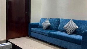 Um quarto com uma porta de madeira escura, um sofá azul com almofadas estampadas e uma mesa de centro preta.