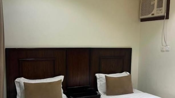Quarto de hotel com duas camas, cabeceira de madeira, ar condicionado fixado na parede e luminária no teto.