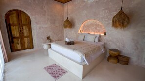 Quarto com cama, mesa de cabeceira e luminária suspensa.