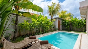 Piscina com espreguiçadeiras, cercada por vegetação tropical exuberante.