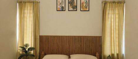 Quarto com cama, cortinas, ar-condicionado e uma pequena mesa com uma planta.