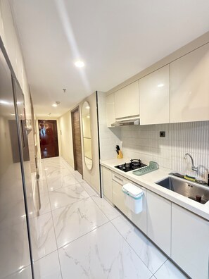 Uma cozinha moderna com armários brancos, uma pia de aço inoxidável e piso de mármore.