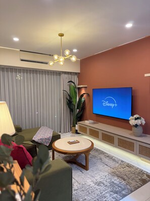 Uma sala de estar moderna com uma televisão exibindo o logotipo do Disney+, um sofá, uma mesa de centro e uma grande planta em vaso.