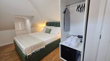 Quarto com cama, guarda-roupa e pequena escrivaninha com toalhas.