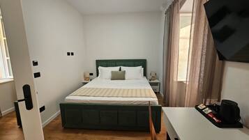 Quarto de hotel com cama, mesas de cabeceira, escrivaninha e janela com cortinas.