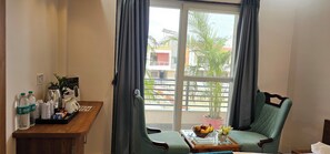 Quarto com escrivaninha de madeira, uma cadeira, uma mesa com uma tigela de frutas e uma janela com cortinas.