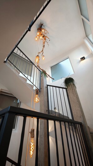 Escadaria com design moderno, apresentando corrimão preto e luminária única feita de galhos e lâmpadas.