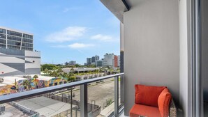 Uma varanda com vista para o horizonte urbano, uma cadeira vermelha e um edifício com um mural colorido.