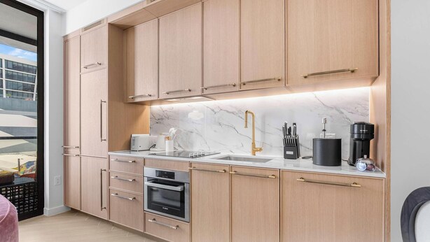 Uma cozinha moderna com armários de madeira, forno Bosch, pia com torneira dourada e máquina de café.