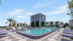 Área de piscina no terraço com espreguiçadeiras, piscina e uma estrutura de prédio moderna.