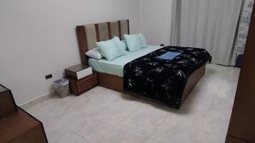 Quarto com cama, mesas de cabeceira, um cesto de lixo e escadas.