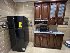 Cozinha compacta com geladeira preta, micro-ondas e armários de madeira.