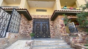 Um edifício com uma entrada decorativa, uma varanda e uma escadaria que leva à entrada.