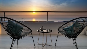 Varanda com duas cadeiras e uma mesa, com vista para o pôr do sol no mar.