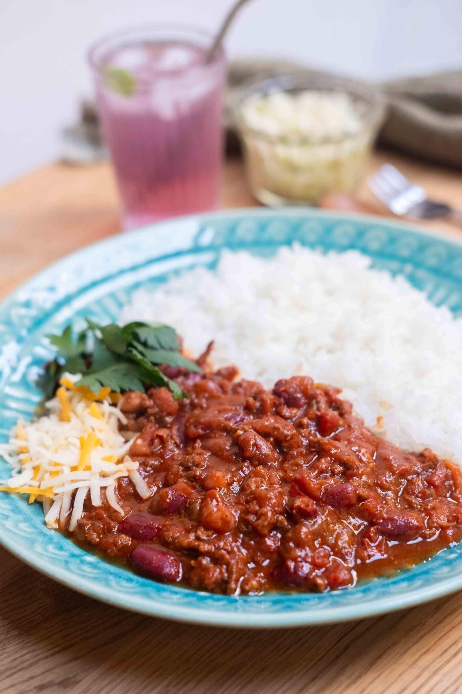 Prato com arroz, feijão e queijo ralado, acompanhado de uma bebida e uma pequena tigela de molho.