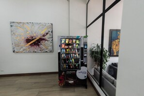 Máquina de vendas com diversos snacks e bebidas, uma garrafa de Coca-Cola e um quadro na parede.