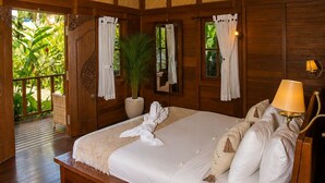 Quarto com cama, ventilador de teto, planta em vaso e vista para o verde lá fora.