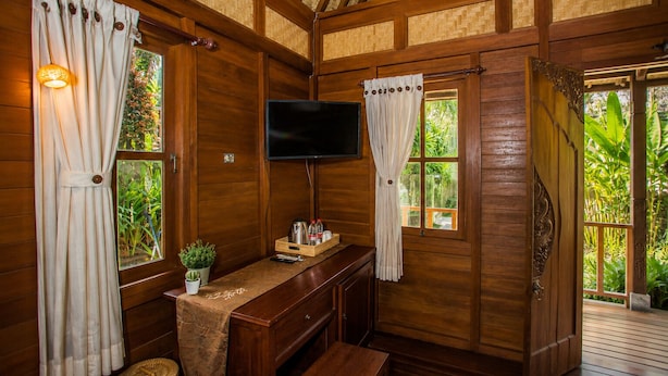 Quarto de madeira com televisão, escrivaninha e janela com cortinas.