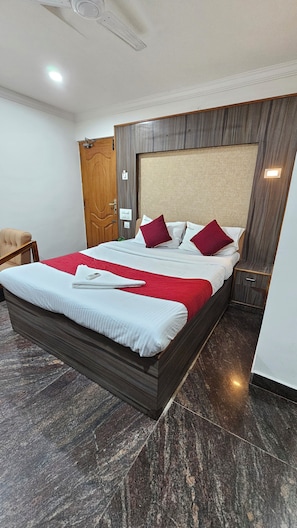 Quarto de hotel moderno com uma cama grande, cabeceira de madeira e piso de mármore.