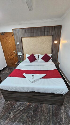 Quarto de hotel com cama grande, cabeceira de madeira e almofada vermelha decorativa.