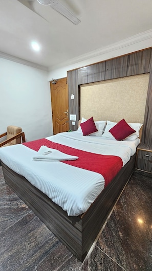 Quarto de hotel com uma cama grande, cabeceira de madeira e edredom vermelho e branco.