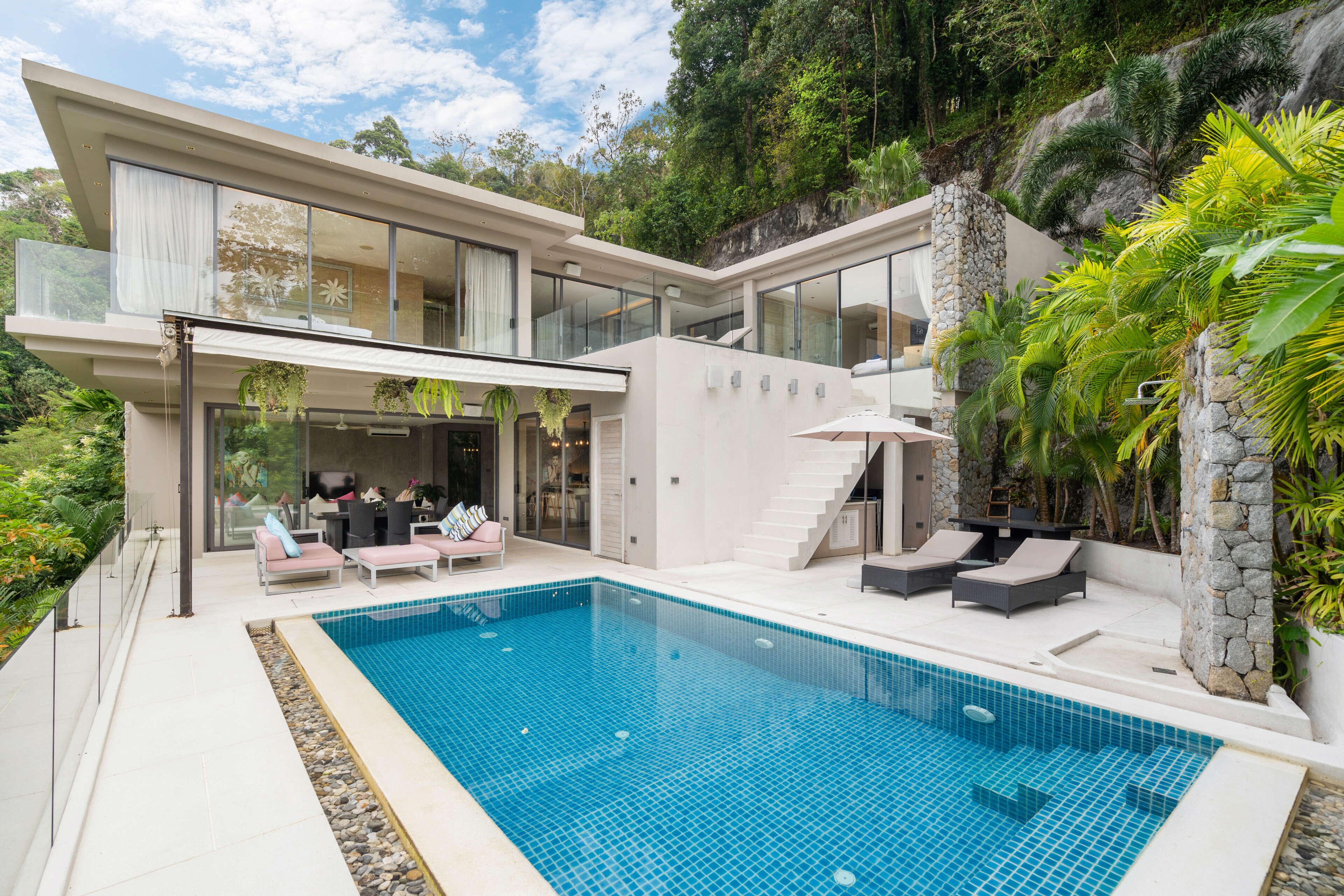 Uma casa moderna com piscina, área de estar externa e escadas que levam a um andar superior.