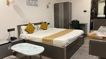 Quarto de hotel com cama, mesa de cabeceira, escrivaninha, cadeira, guarda-roupa e uma pequena mesa com cadeira.
