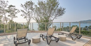 Varanda com duas cadeiras de descanso e uma mesa pequena, com vista para a água e vegetação.