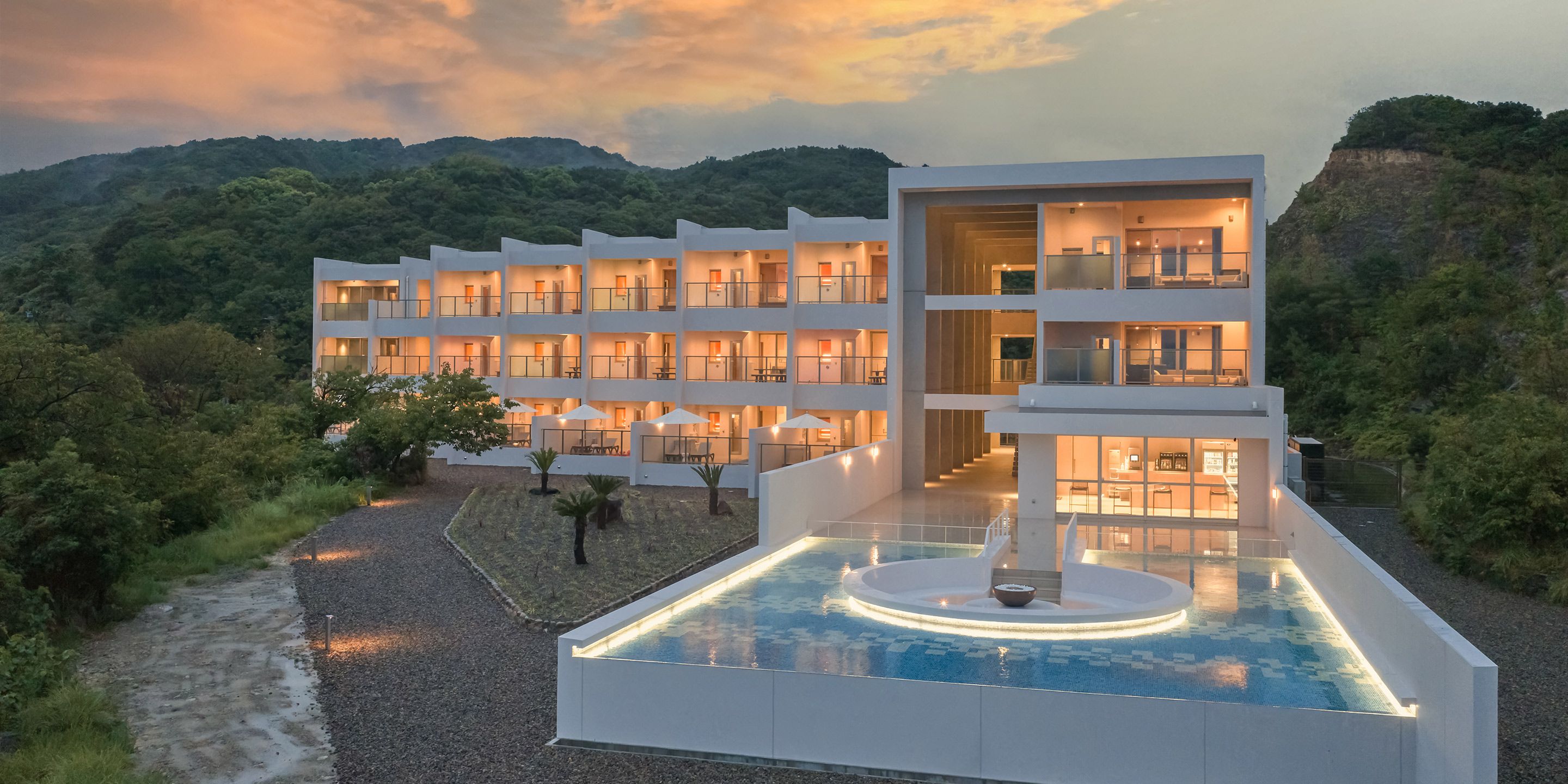 Hotel moderno com vários andares, piscina e vista para as colinas arborizadas ao redor.