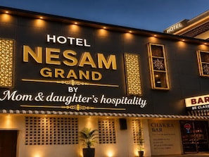 Um hotel chamado 'Nesam Grand' com uma placa indicando 'Hospitalidade de mãe e filha'.