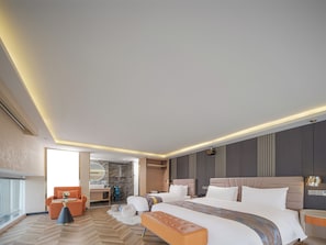 Quarto de hotel moderno com uma cama grande, área de estar com uma poltrona e uma mesinha, banheiro com espelho e pia, e vista através de uma janela ampla.