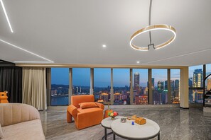 Sala de estar moderna com vista para a cidade, um sofá, uma poltrona e uma mesa de centro com objetos decorativos.