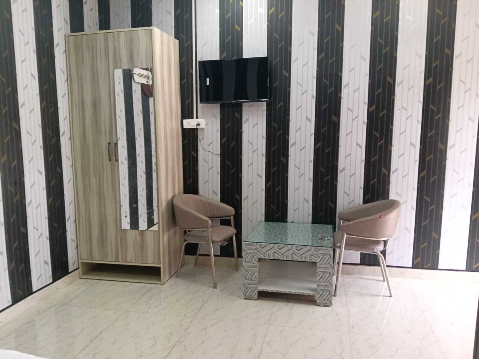 Quarto com guarda-roupa, duas cadeiras, uma mesinha e televisão.