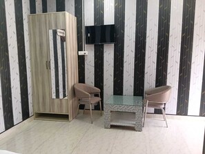 Quarto com guarda-roupa, duas cadeiras, uma mesinha e televisão.