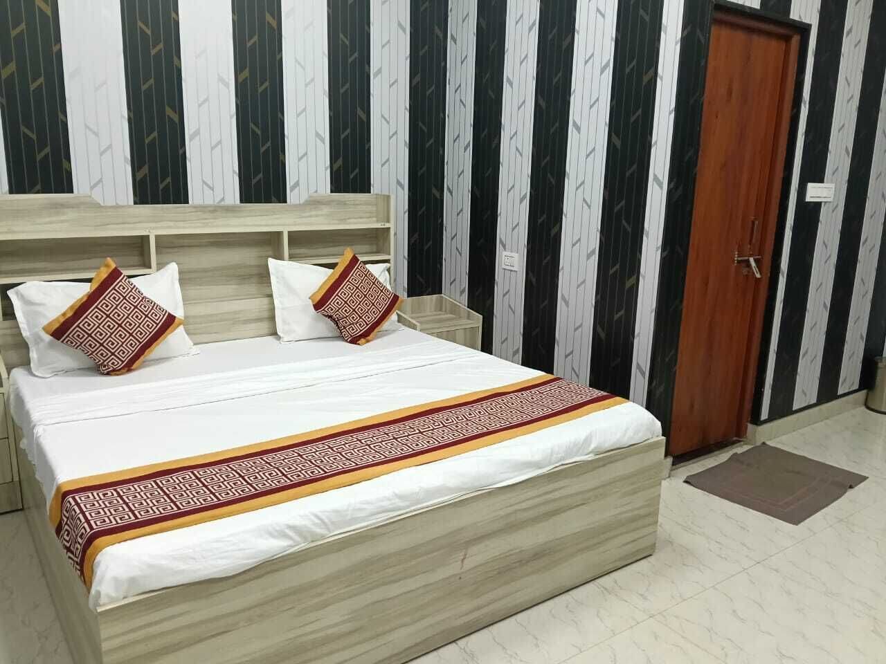 Uma cama com colcha estampada e almofadas, uma cabeceira de madeira e um padrão listrado na parede.