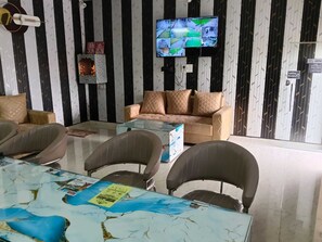 Sala de estar com sofá, cadeiras, mesa de centro e televisão exibindo diversas câmeras.