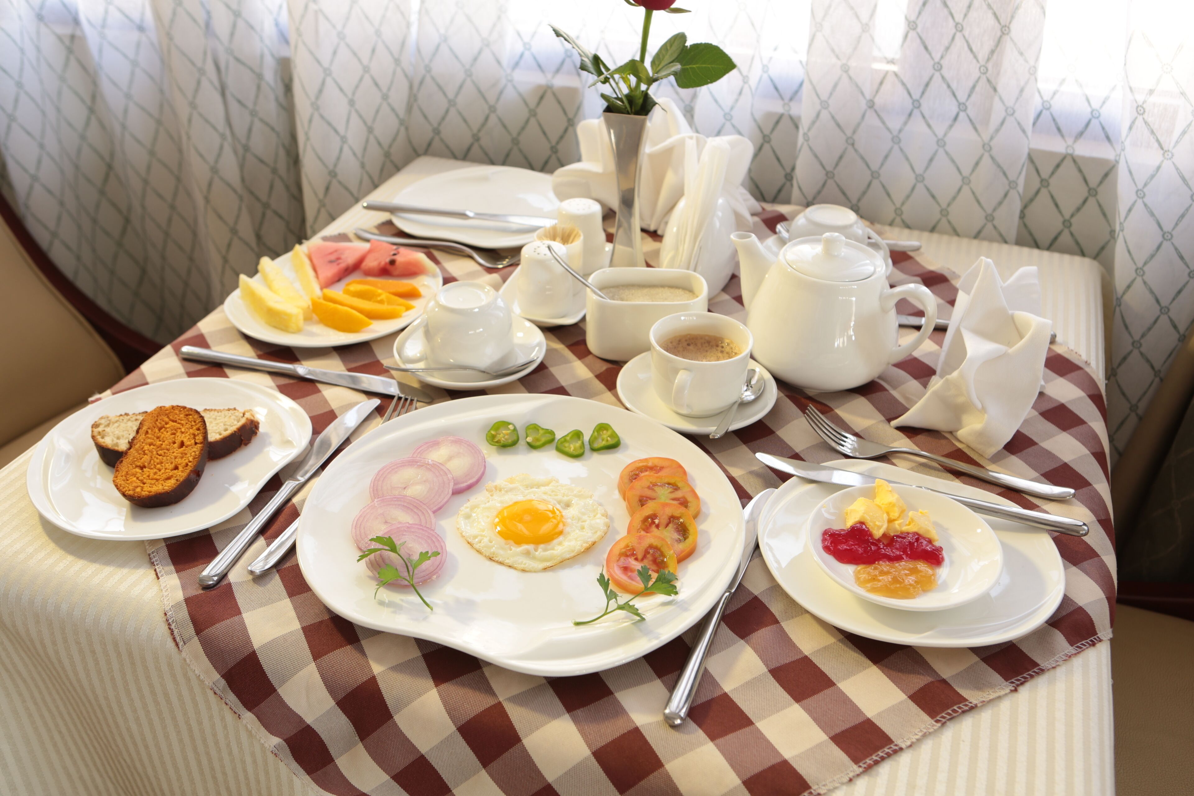 Mesa de café da manhã com pratos de comida, talheres e um bule de chá.
