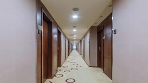 Corredor de hotel com portas em ambos os lados, carpete com padrões circulares e iluminação no teto.