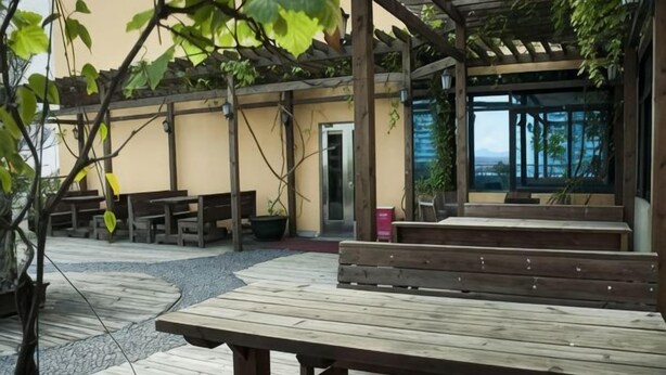 Um pátio externo com bancos e mesas de madeira, uma estrutura de pérgola e vista para o mar.