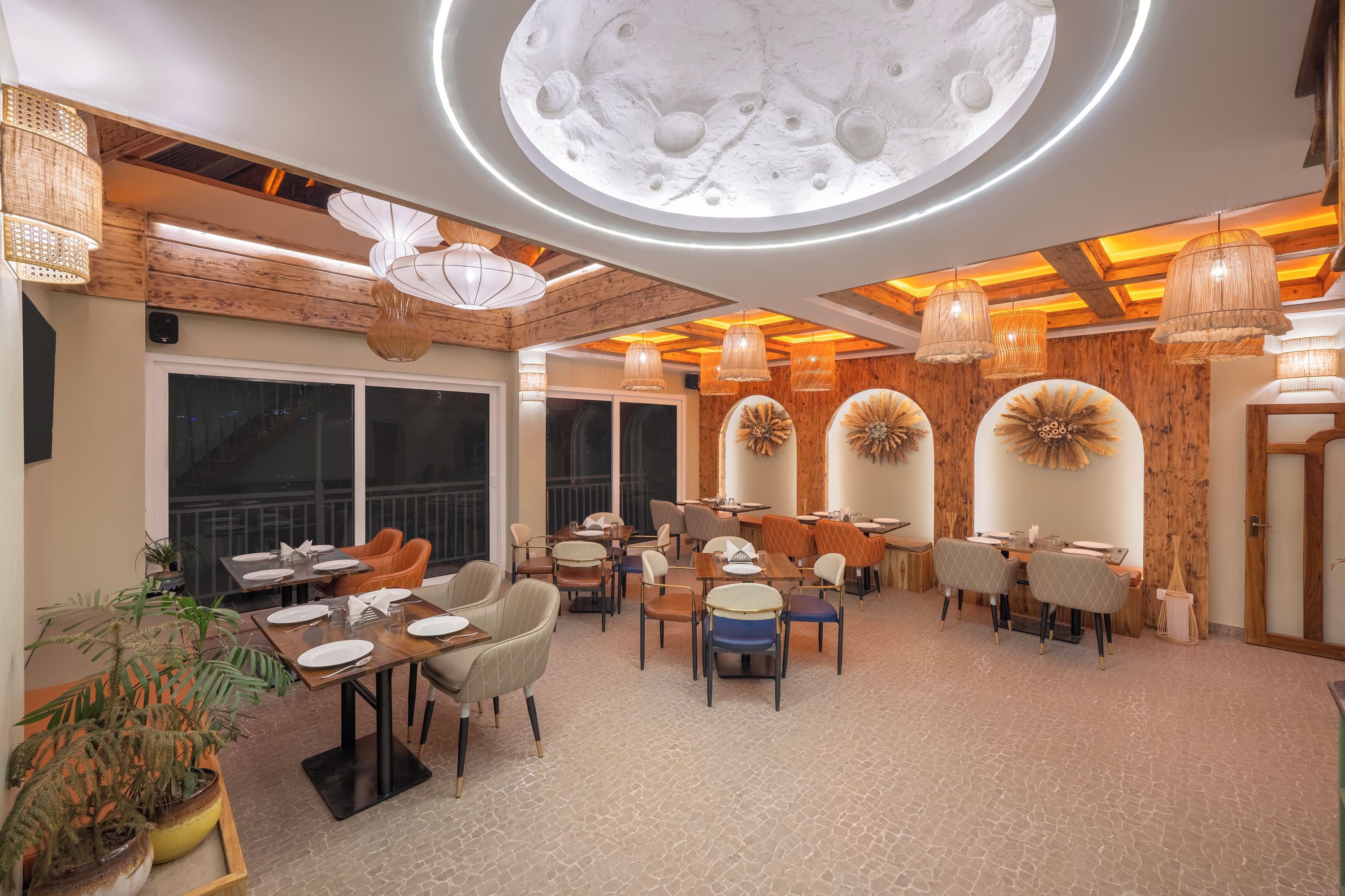 Um restaurante com várias mesas e cadeiras, luminária circular no teto e painéis de madeira nas paredes.