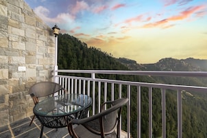 Varanda com mesa de vidro e cadeiras de vime, com vista para uma paisagem montanhosa.