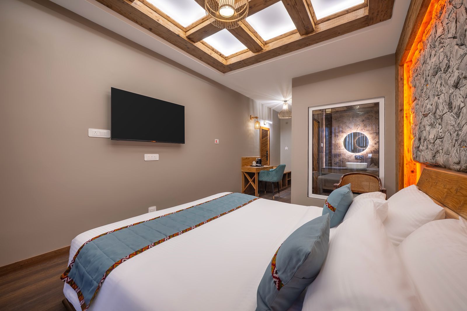 Quarto de hotel com uma cama grande, televisão, escrivaninha com cadeira e banheiro com espelho e pia.