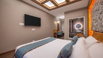 Quarto de hotel com uma cama grande, televisão, escrivaninha com cadeira e banheiro com espelho e pia.