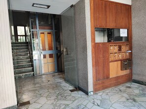 Um saguão com escada, um armário de madeira com vários compartimentos e piso ladrilhado.